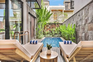 Área de piscina com espreguiçadeiras e uma pequena mesa, cercada por vegetação e paredes de pedra.