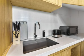 Uma cozinha com pia de aço inoxidável, porta-facas, cafeteira e micro-ondas.