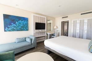 Quarto de hotel com cama, área de estar, escrivaninha, televisão e banheiro.