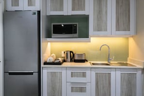 Cozinha compacta com geladeira de aço inoxidável, micro-ondas, chaleira, torradeira e pia.