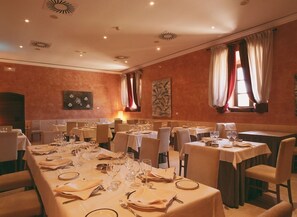 Uma sala de jantar com várias mesas preparadas para o serviço, um candelabro e obras de arte nas paredes.