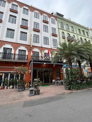 Um hotel de vários andares com entrada no nível da rua, área de estar ao ar livre e diversos vasos de plantas.