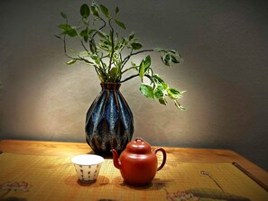 Um vaso de cerâmica com uma planta, um bule e uma chávena sobre uma mesa.