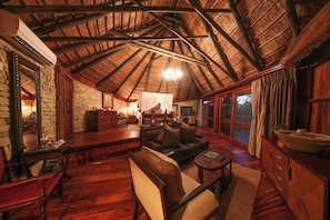 Um interior acolhedor com teto de madeira alto, paredes de pedra e uma área de estar confortável com sofá e poltronas.