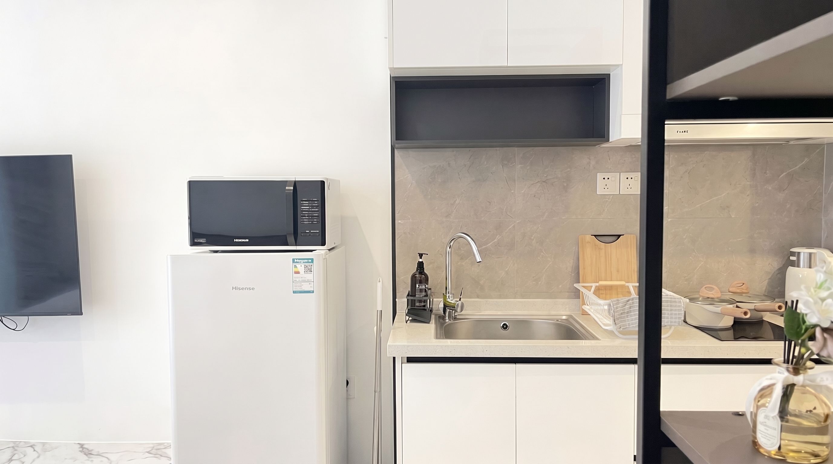 Cozinha compacta com micro-ondas, pia e geladeira pequena.