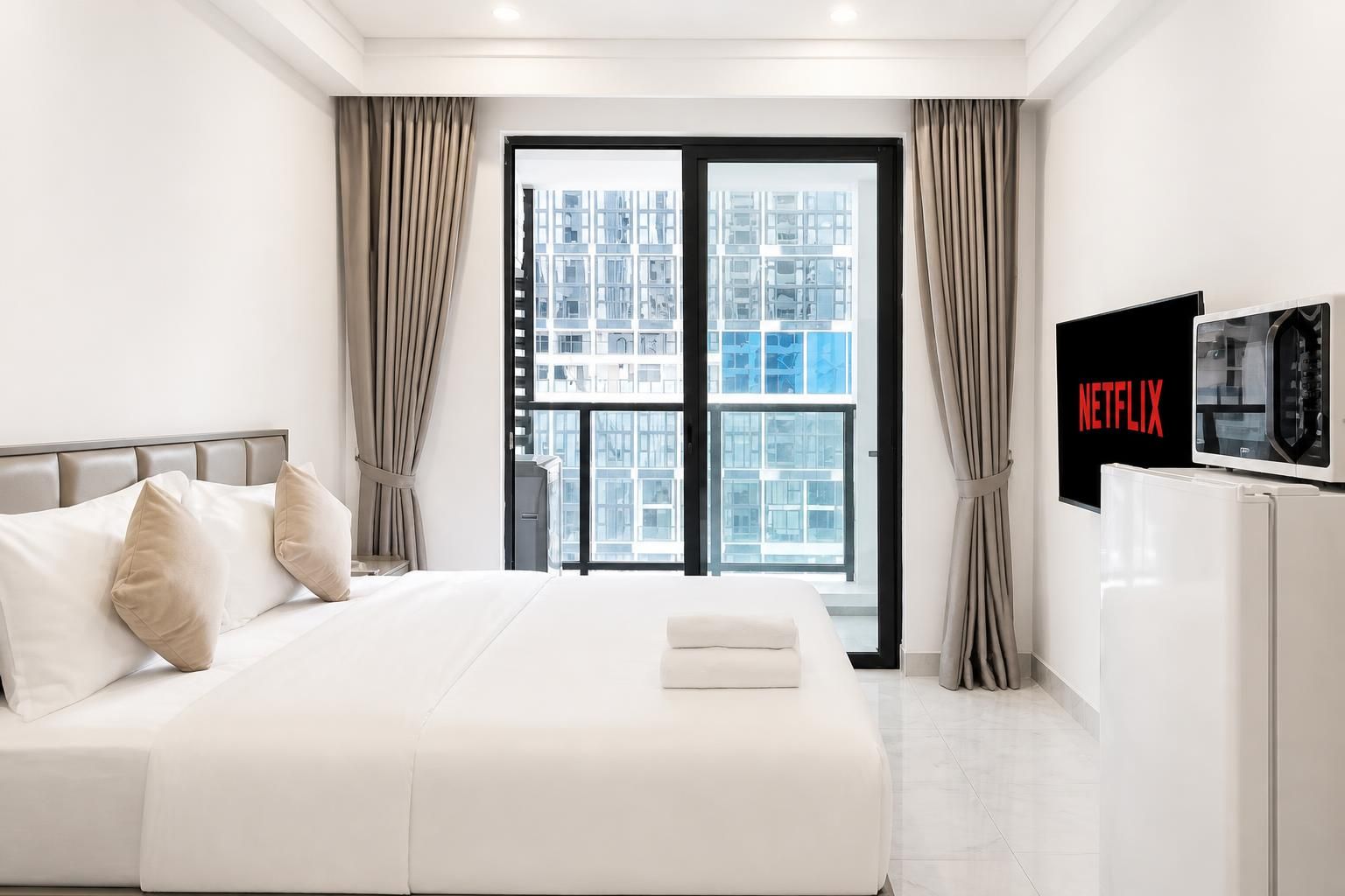 Quarto de hotel com uma cama grande, televisão e vista para um edifício pela janela.