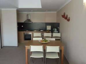 Cozinha moderna com forno embutido, fog ão e exaustor. Há uma mesa de jantar com quatro cadeiras e uma fruteira em cima.