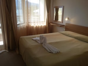 Quarto de hotel com cama, cortinas, espelho e janela.