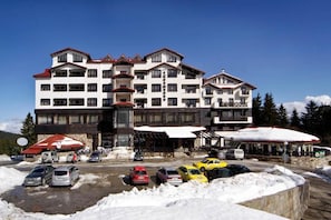 Hotel com vários andares, área de estacionamento em frente, com diversos carros e um espaço coberto para área externa.