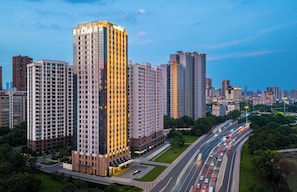 Um hotel moderno e alto, com uma placa chamativa, rodeado por outros edifícios imponentes e uma estrada movimentada.