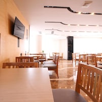 Um espaço de refeições de hotel com mesas e cadeiras de madeira, uma TV de tela plana na parede e um design moderno no teto.