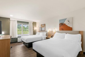 Quarto de hotel com duas camas, uma escrivaninha, janela com cortinas, luminárias na parede e um quadro.