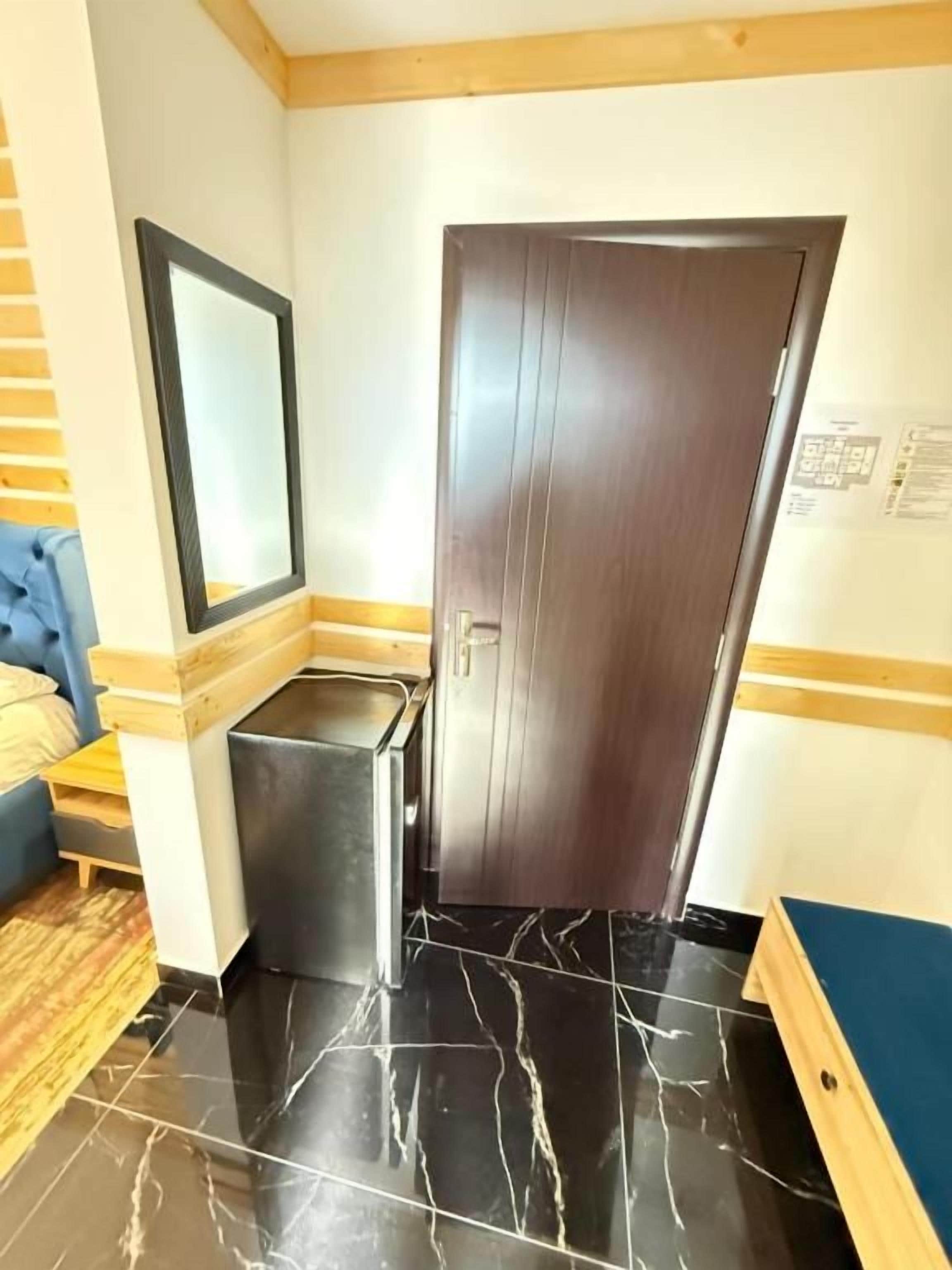 Um quarto com porta de madeira escura, um pequeno armário preto, um espelho na parede e um sofá azul.