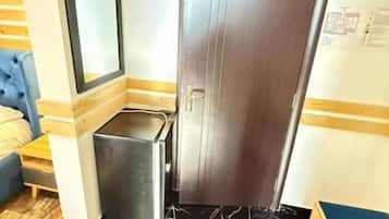Um quarto com porta de madeira escura, um pequeno armário preto, um espelho na parede e um sofá azul.