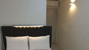 Cama bem arrumada com roupa de cama e almofadas brancas, cabeceira e luminária fixada na parede.