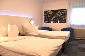 Quarto de hotel com duas camas, uma escrivaninha, uma cadeira e um quadro abstrato grande na parede.