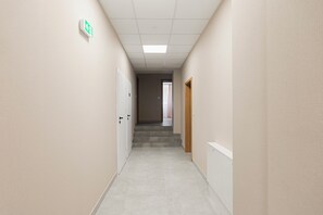 Um corredor iluminado no teto, uma porta com puxador e uma escadaria que dá para outro cômodo.