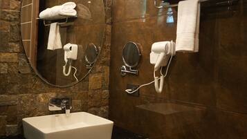 Casa de banho com lavatório branco, espelho redondo, secador de cabelo portátil e suporte para toalhas.