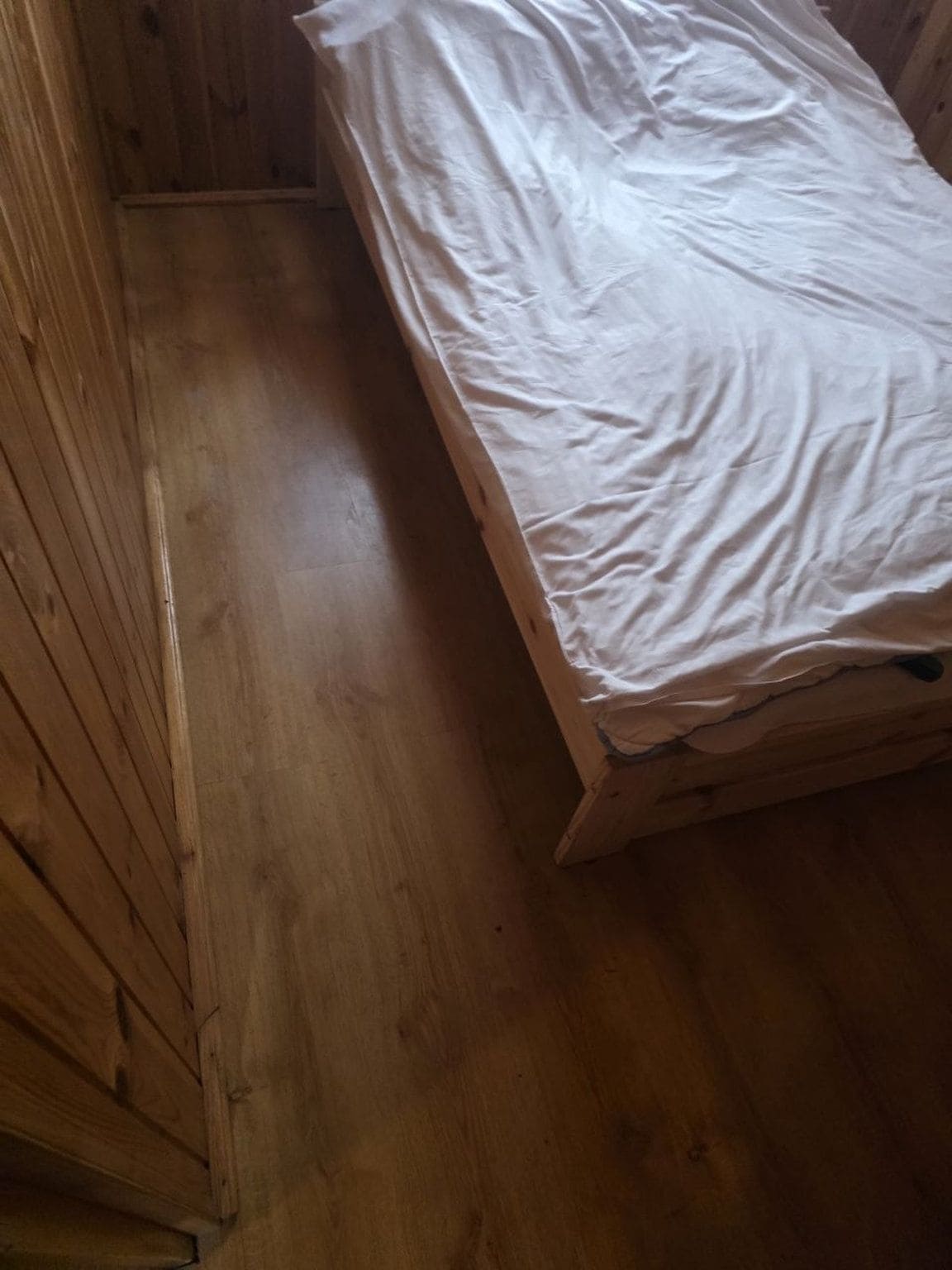 Piso de madeira com uma cama encostada na parede.