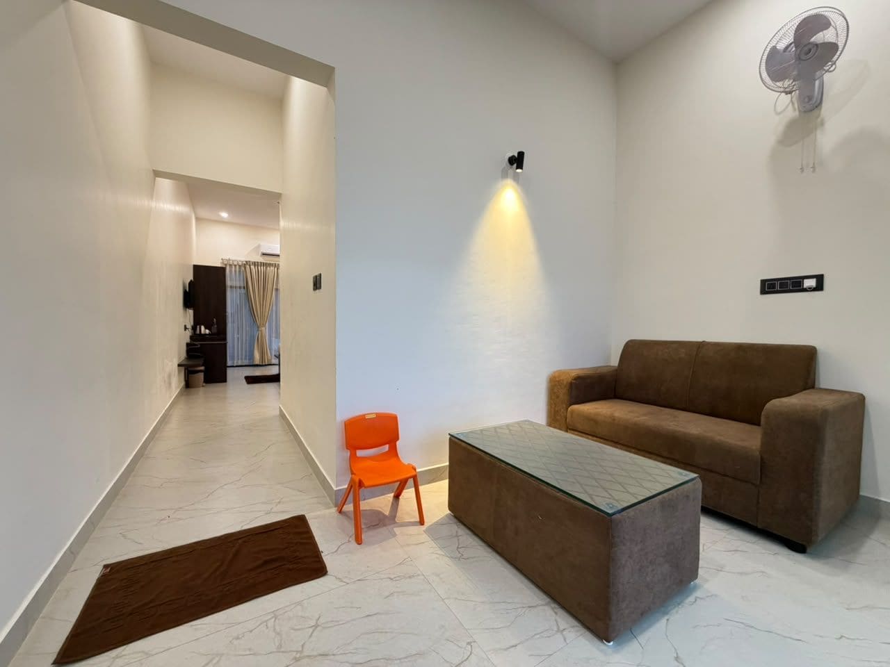 Uma sala de estar moderna com um sofá, uma mesa de centro de vidro e uma pequena poltrona laranja.