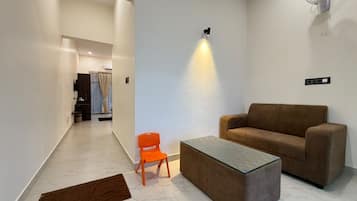 Uma sala de estar moderna com um sofá, uma mesa de centro de vidro e uma pequena poltrona laranja.