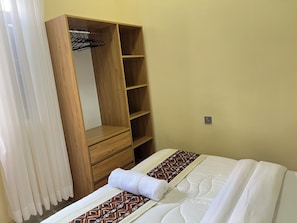 Quarto de hotel com cama, guarda-roupa de madeira, espelho e tomada na parede.
