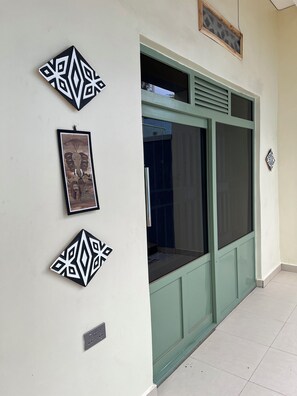 Entrada de um edifício com porta verde, moldura de quadro fixada na parede e um elemento decorativo.