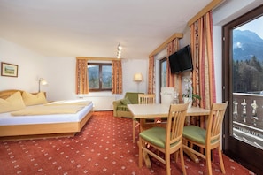 Quarto de hotel com cama, mesa e cadeiras, televisão e janela com cortinas.