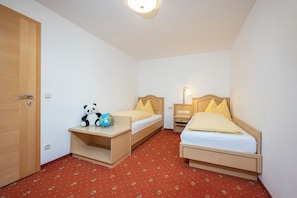 Um quarto pequeno com duas camas de solteiro, uma escrivaninha de madeira com um globo e um panda de pelúcia, e uma porta.