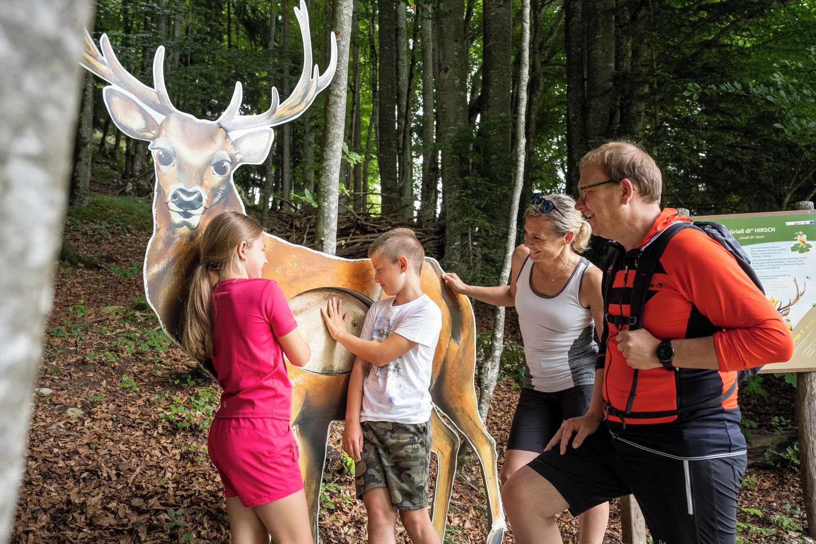 Um grupo de pessoas interagindo com uma escultura de veado em uma área arborizada.