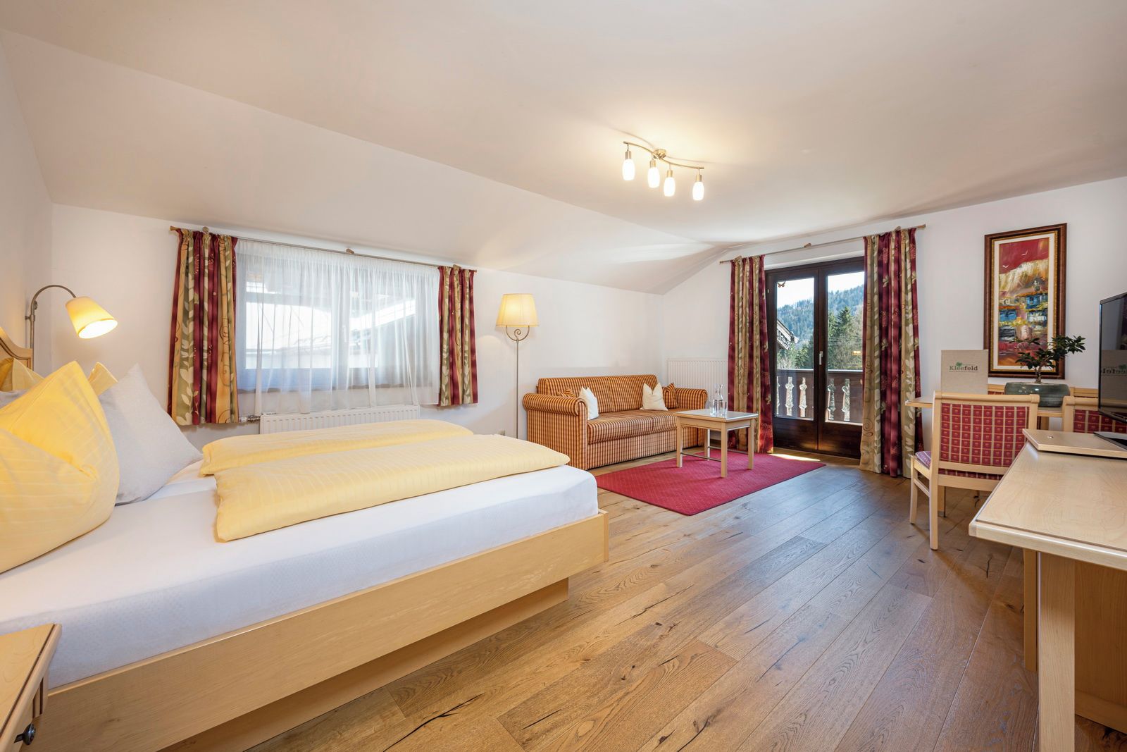 Quarto de hotel com cama, sofá, mesa e televisão.
