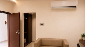 Quarto com sofá bege, porta de madeira, armário e ar-condicionado fixado na parede.