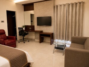 Quarto de hotel com cama, escrivaninha, cadeira, televisão e sofá.