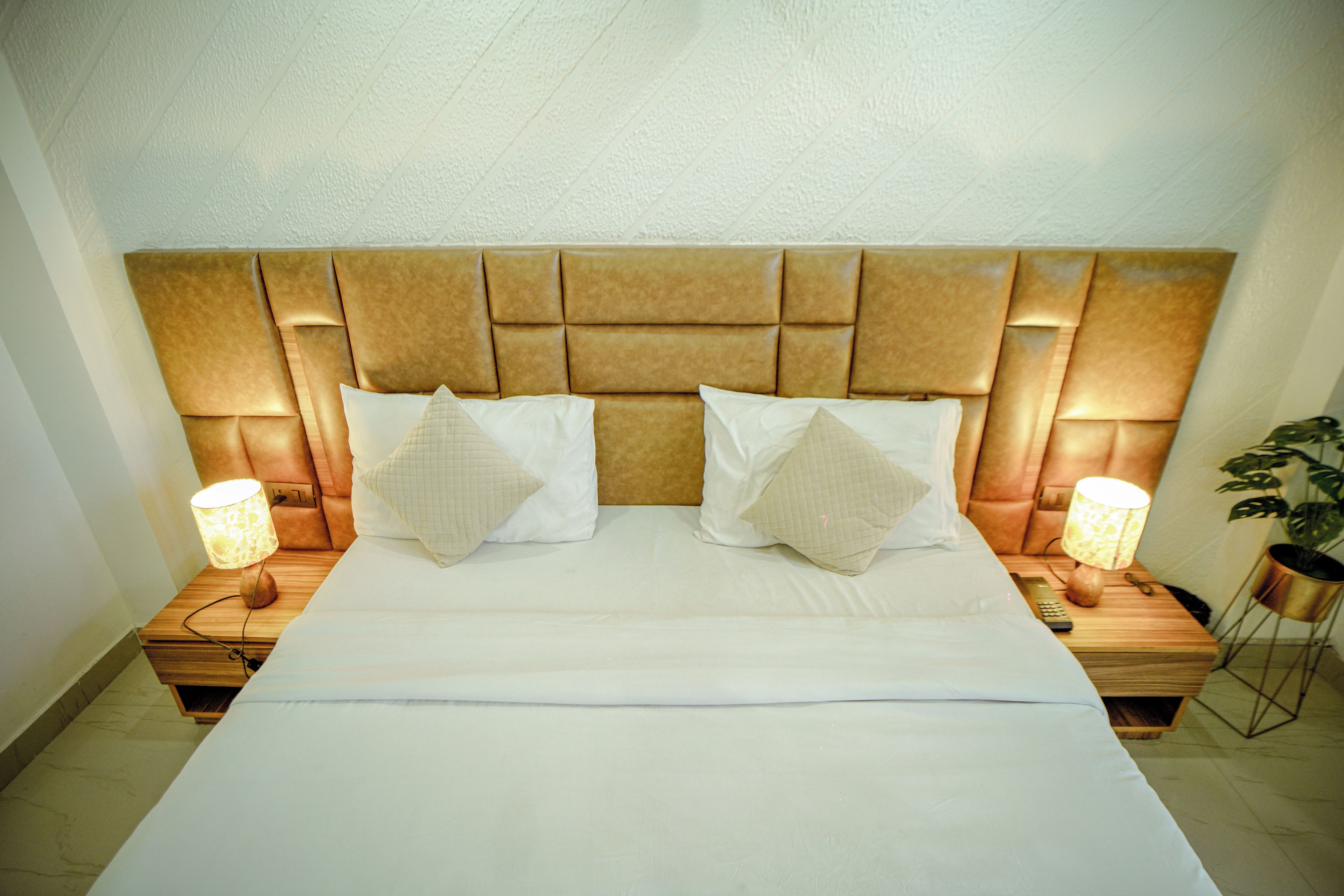 Quarto de hotel com uma cama grande, duas luminárias de cabeceira e cabeceira com padrão geométrico.