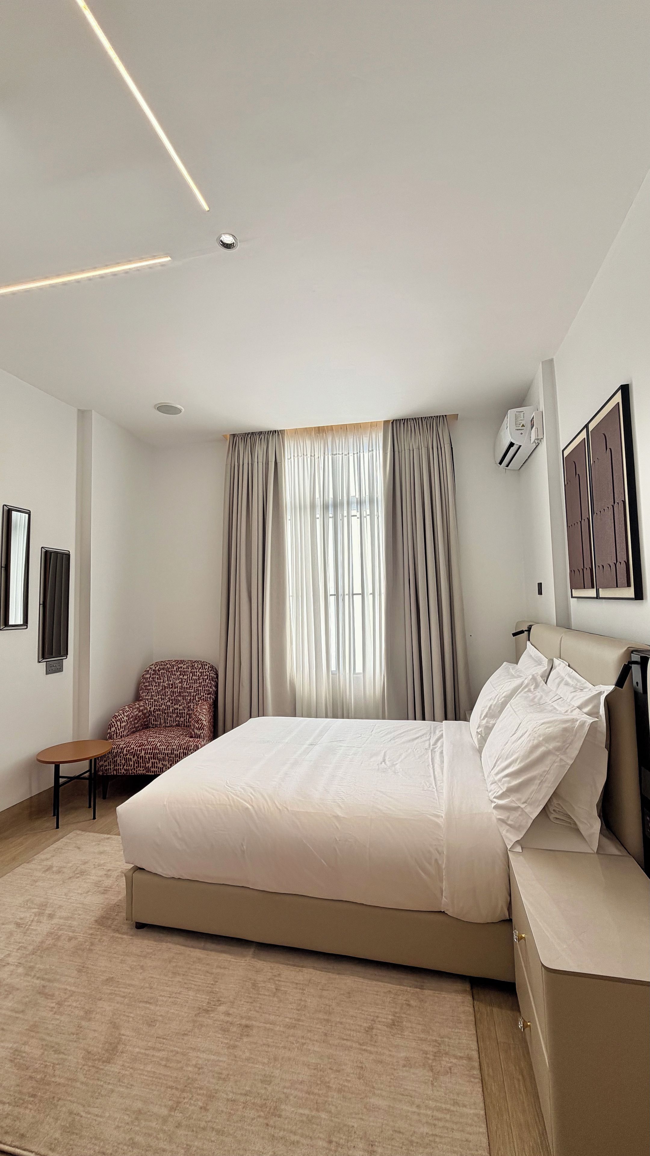 Quarto moderno com cama grande, uma cadeira e janela com cortinas.