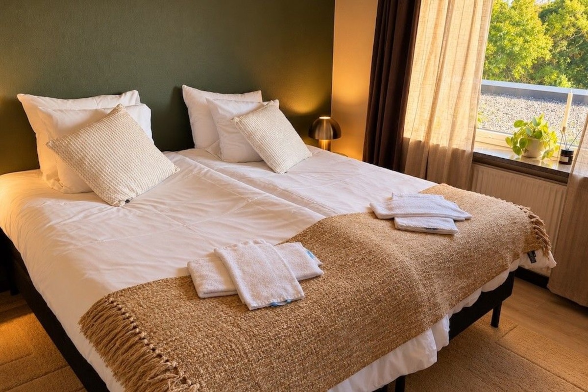 Uma cama de casal com roupa de cama branca, um cobertor bege e duas toalhas.