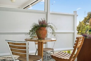 Mesa redonda com um vaso de terracota em cima, duas cadeiras de madeira e uma parede branca ao fundo.