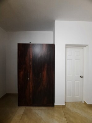 Quarto com armário de madeira escura, porta branca e chão de azulejos.
