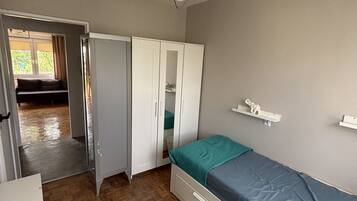 Quarto com cama, guarda-roupa, espelho, prateleira com uma estátua e porta que dá para outro cômodo.
