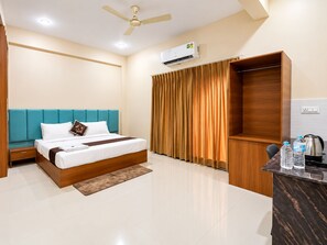 Quarto de hotel com cama, escrivaninha, guarda-roupa, ventoinha no teto e ar condicionado.