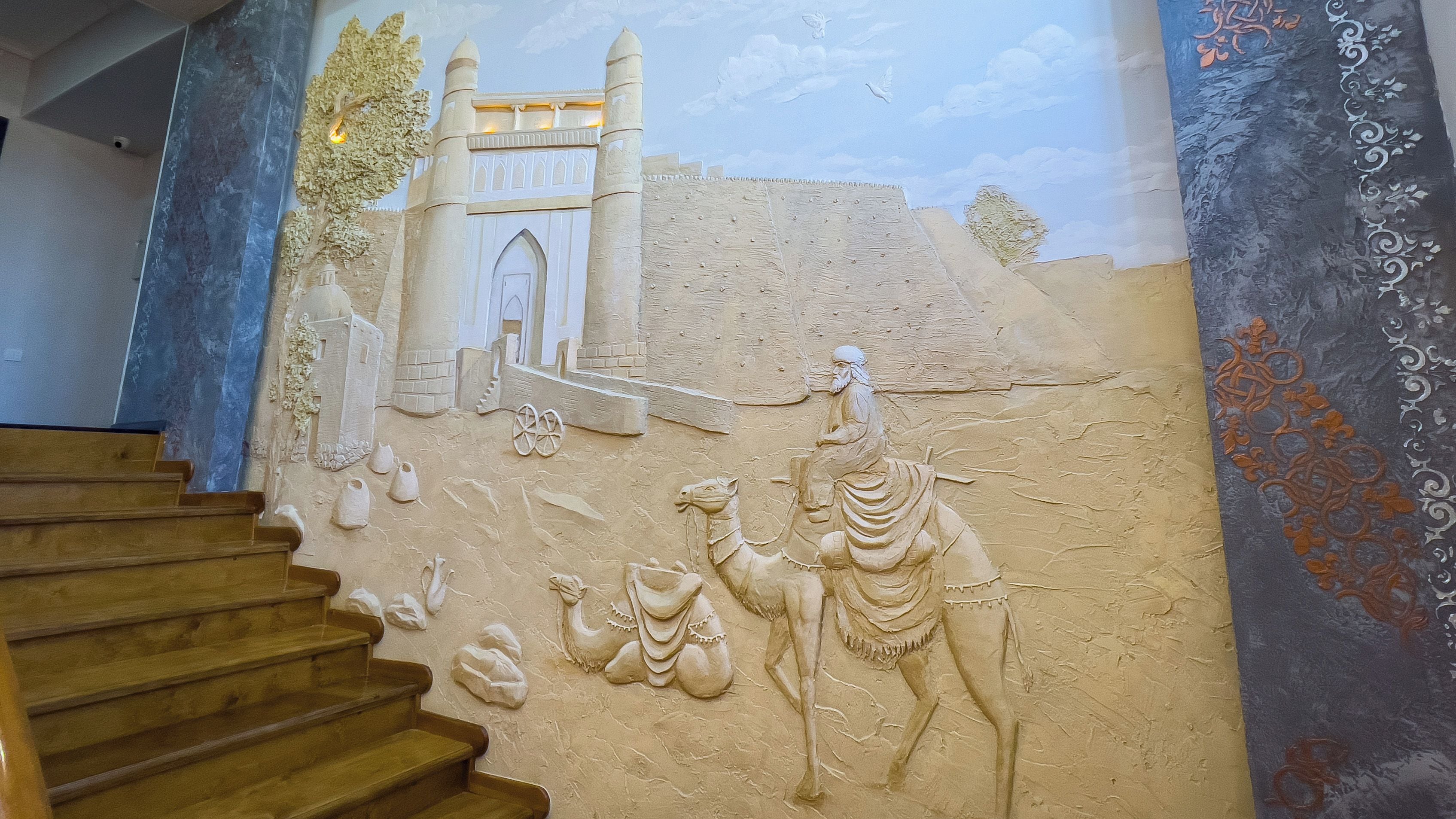 Uma escadaria com um mural que retrata uma cena histórica, com um castelo, um homem em um camelo e uma paisagem desértica.