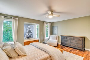 Quarto com cama, penteadeira, janela com cortinas e ventilador de teto.