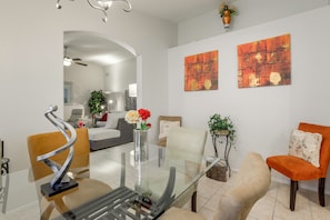 Uma sala de estar moderna com uma mesa de jantar de vidro, assentos confortáveis e duas pinturas abstratas na parede.