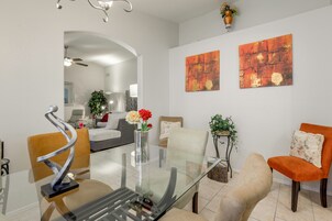 Uma sala de estar moderna com uma mesa de jantar de vidro, assentos confortáveis e duas pinturas abstratas na parede.