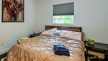 Um quarto com cama, mesa de cabeceira, janela e um quadro na parede.