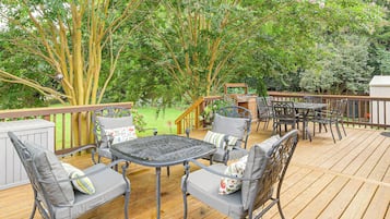 Um pátio externo com deck de madeira, mesa de metal e cadeiras com almofadas.
