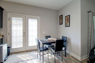 Uma área de refeições com uma mesa, cadeiras, uma porta com janela e uma parede com duas imagens emolduradas.