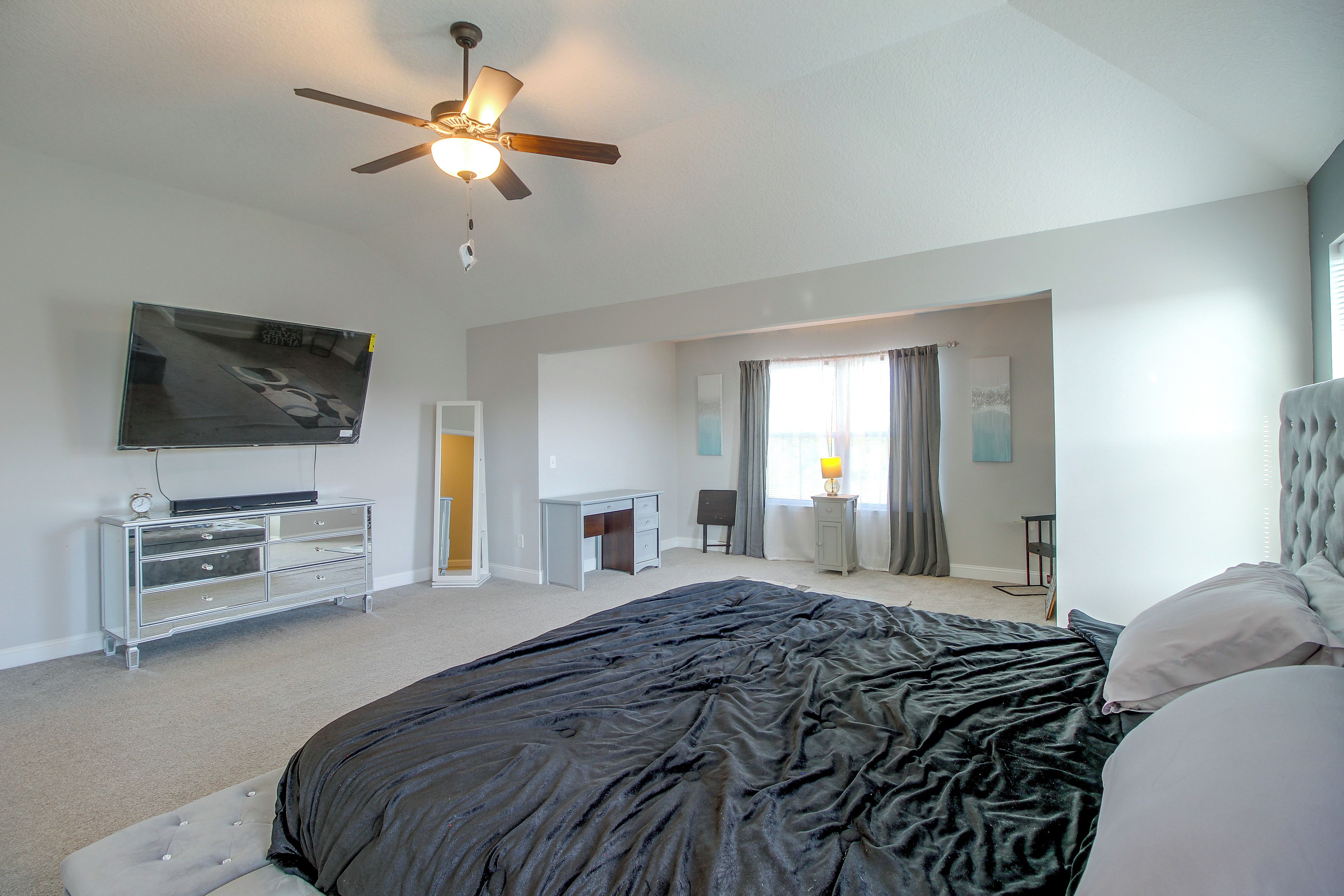 Quarto com cama, ventilador de teto, televisão, cômoda e escrivaninha.