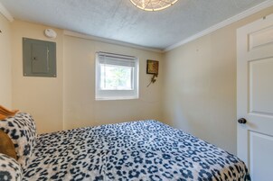 Quarto com cama, janela, luminária na parede e porta.