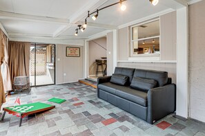 Sala de estar com sofá preto, piso quadriculado verde e vermelho, luminária no teto e janela com vista.